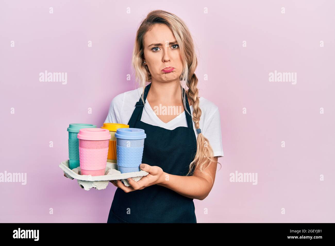 Beautiful young blonde woman wearing waitress apron holding take away ...