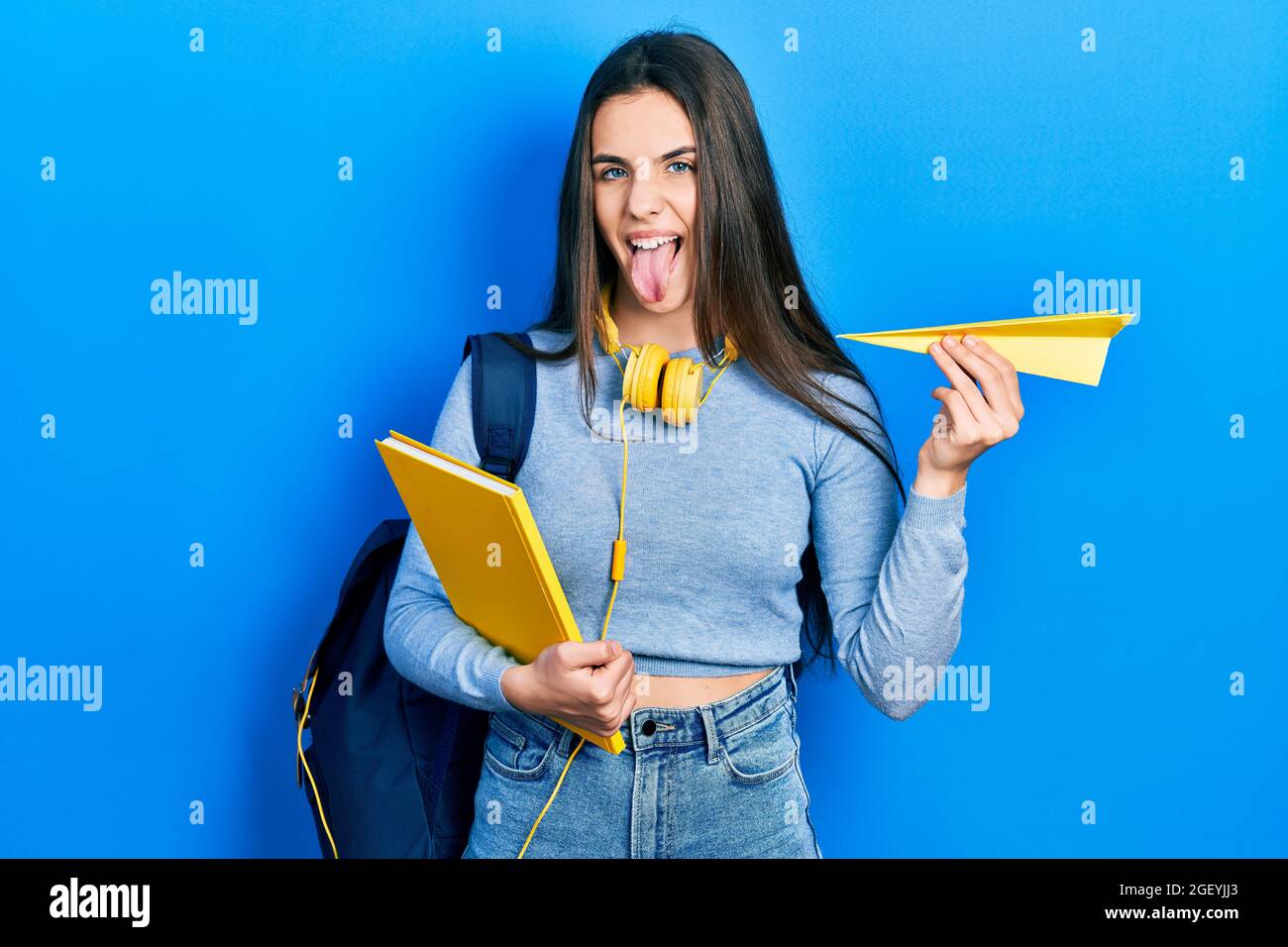Young brunette teenager student holding books and paper plane sticking ...