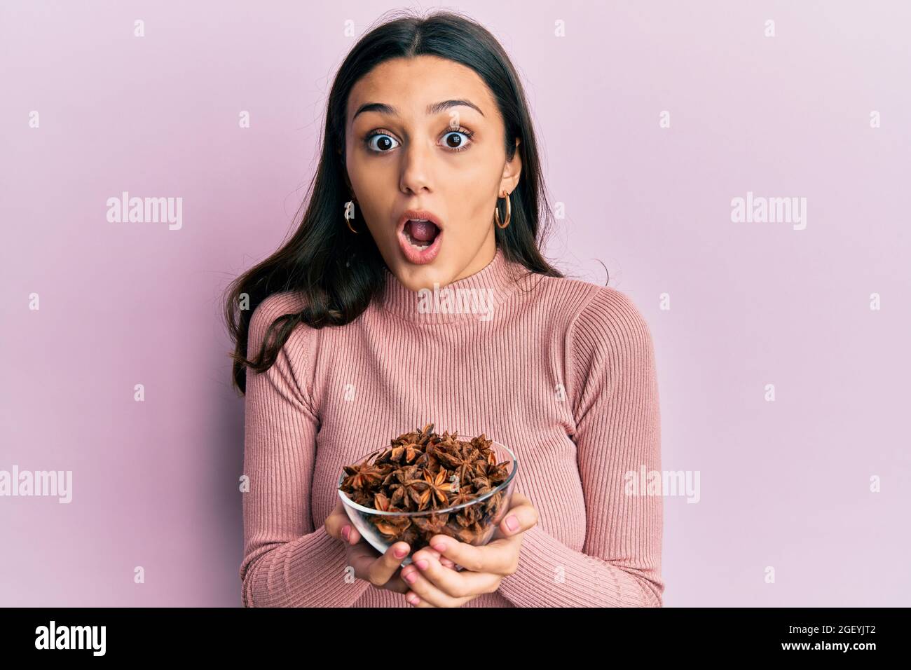 Young hispanic woman holding bowl of star anise afraid and shocked with ...