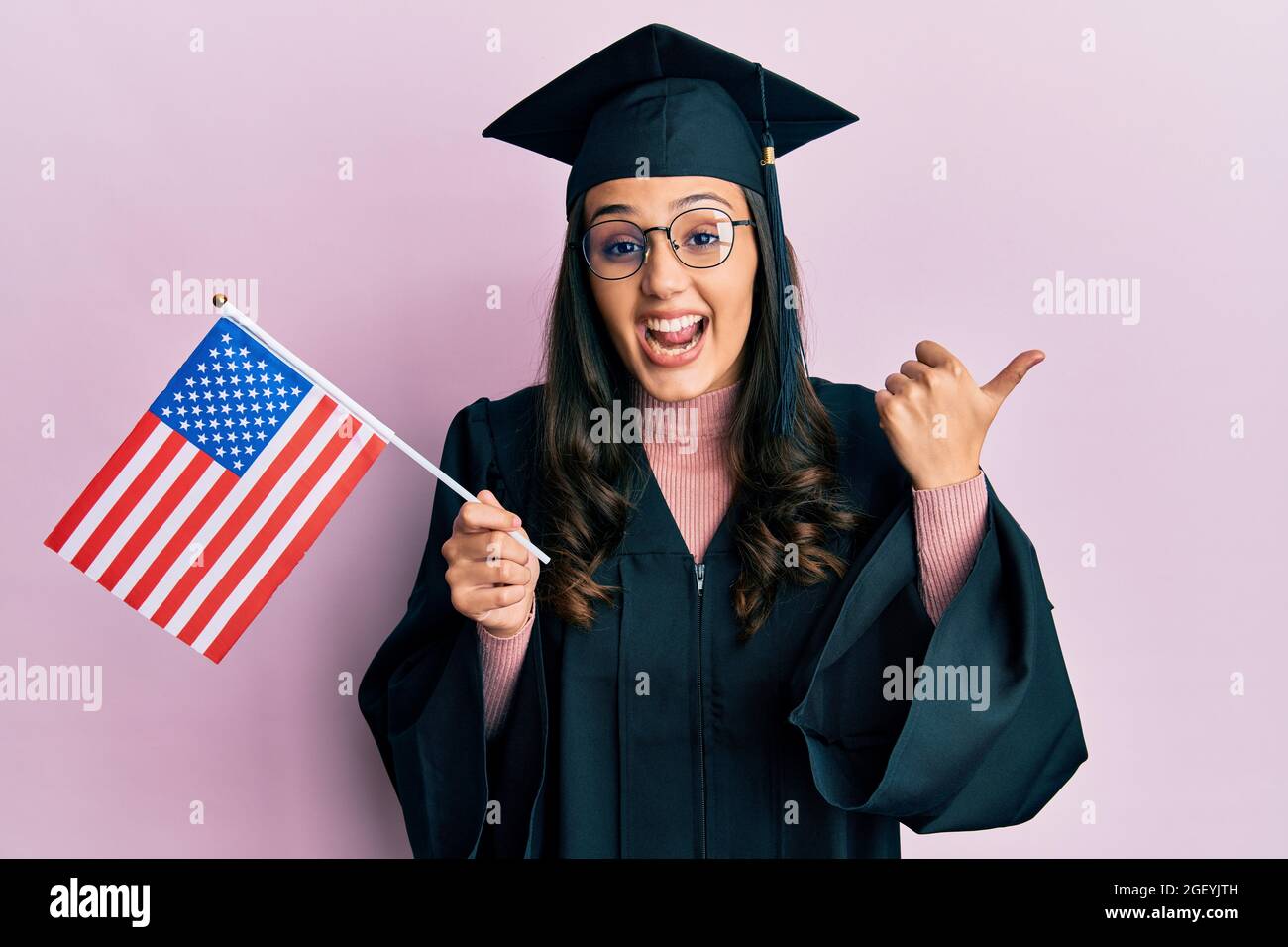 Young hispanic woman wearing graduation cap and ceremony robe holding ...