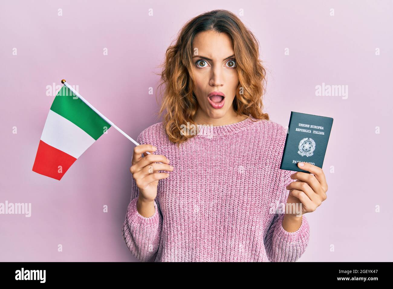 Young caucasian woman holding italy flag and passport in shock face ...
