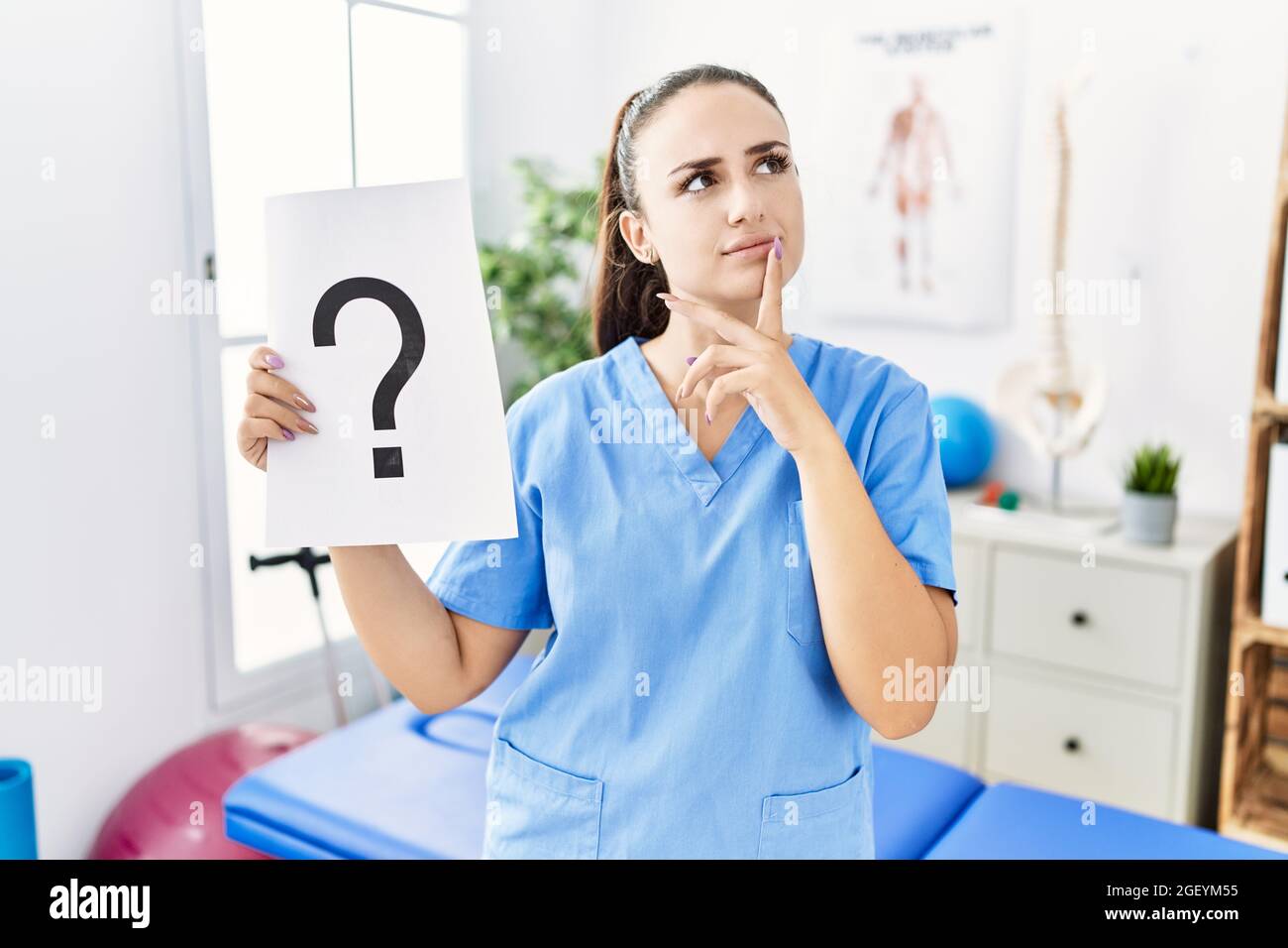 Young physiotherapist woman holding question mark serious face thinking ...