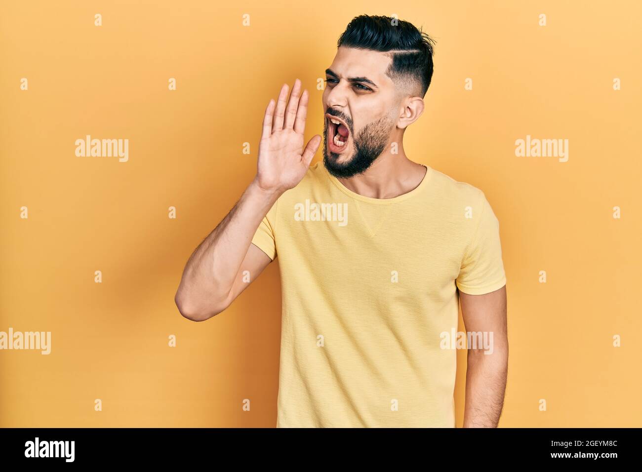 Handsome man with beard wearing casual yellow t shirt shouting and ...