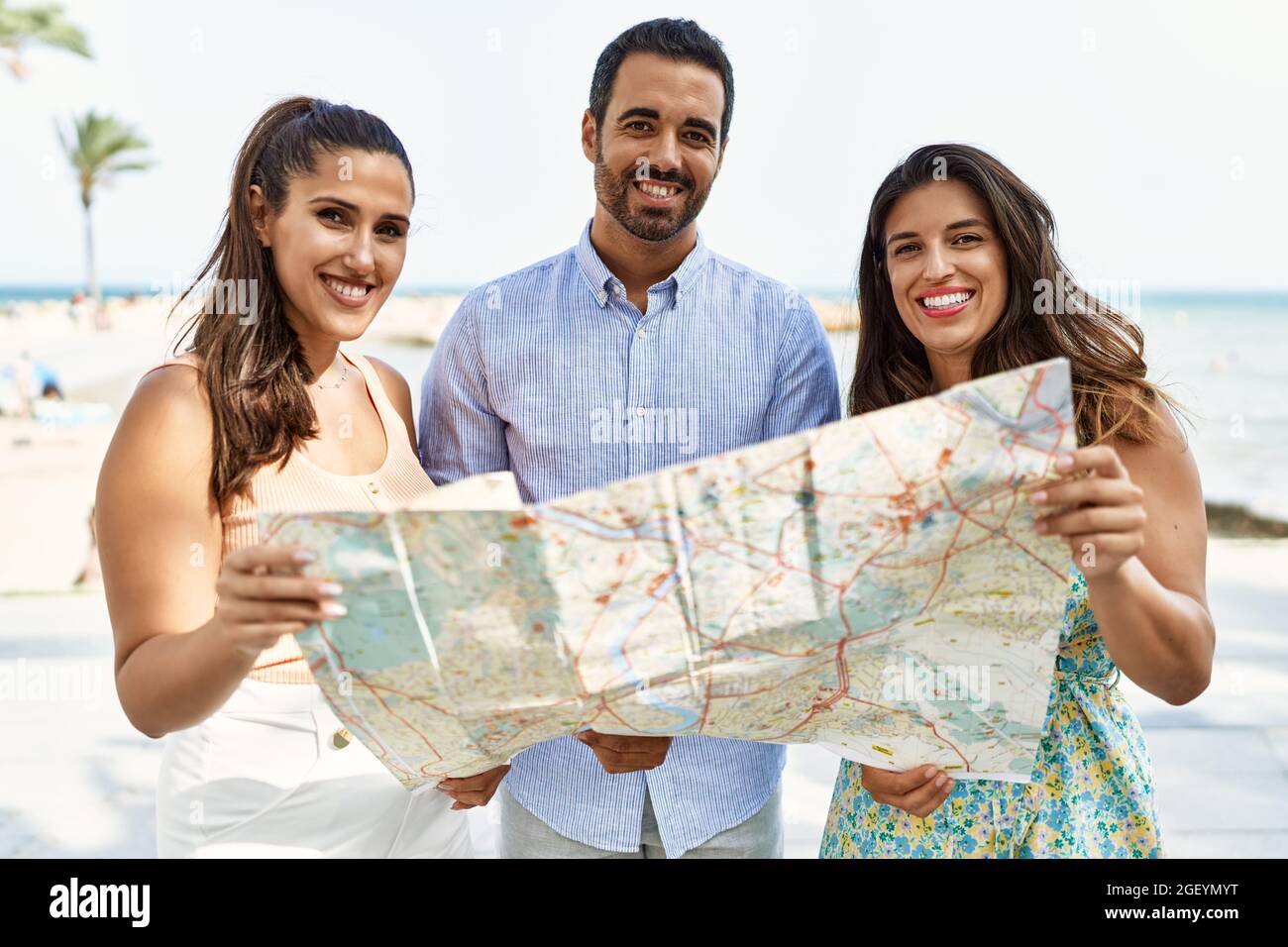 Three young hispanic friends smiling happy searching route on city map ...
