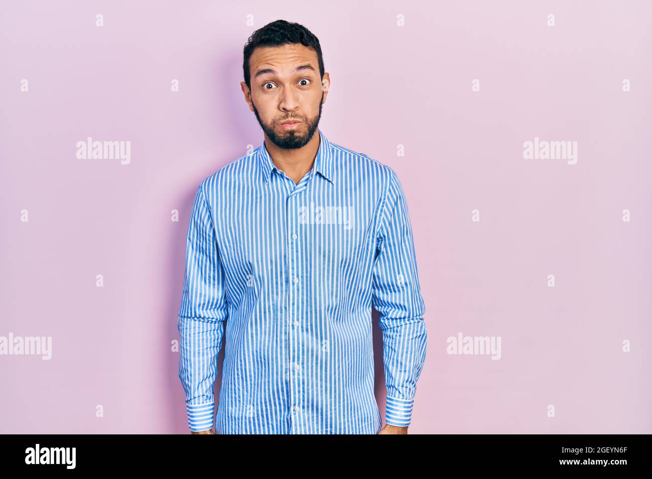 Hispanic man with beard wearing casual blue shirt puffing cheeks with ...