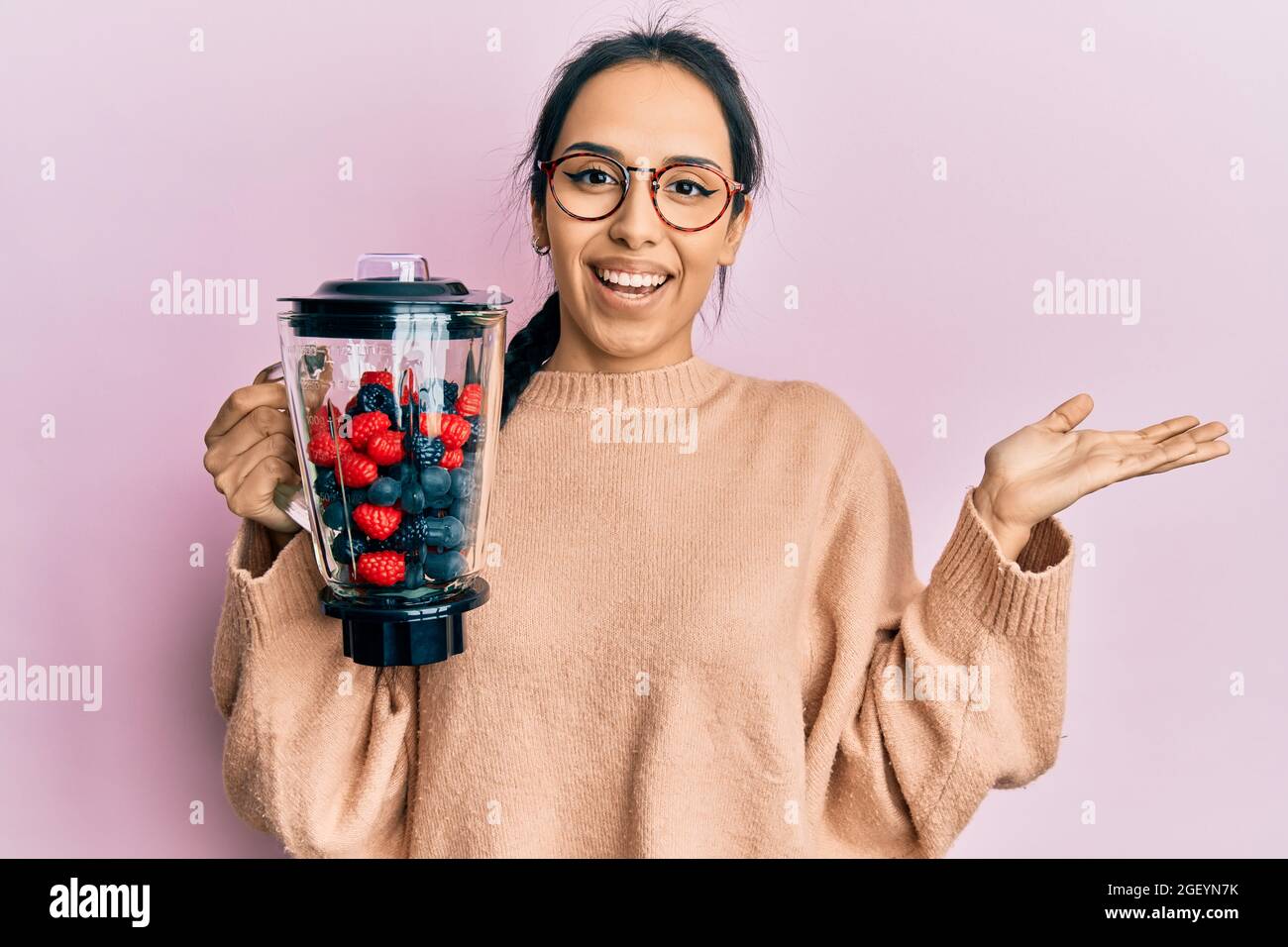 Young hispanic girl holding food processor mixer machine with fruits ...