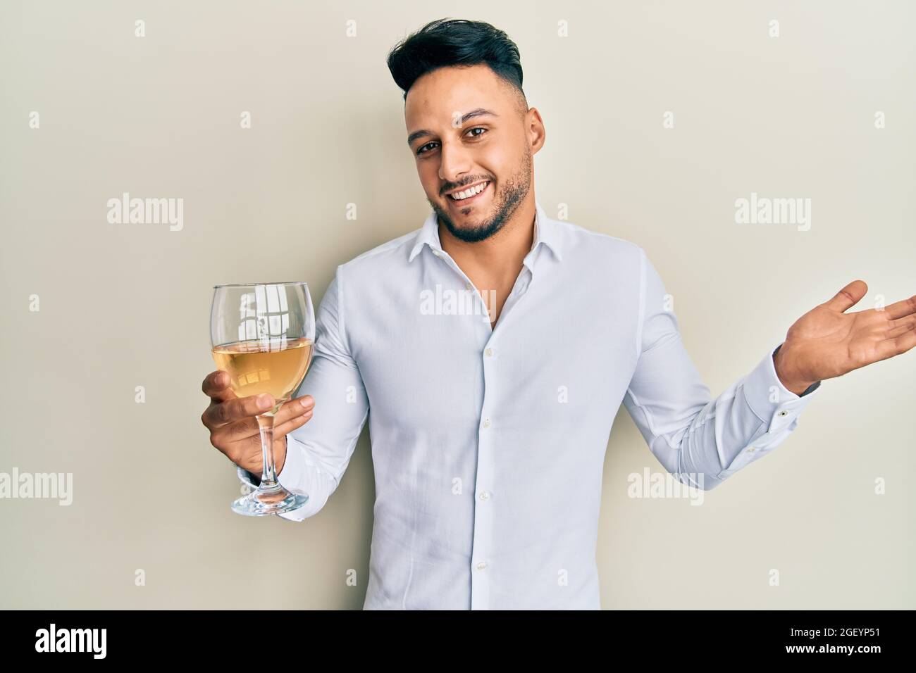 Young arab man drinking a glass of white wine celebrating achievement ...