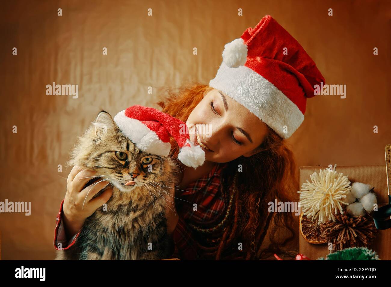 Red-haired female with dreadlocks in Santa Claus hat holds fluffy tabby ...