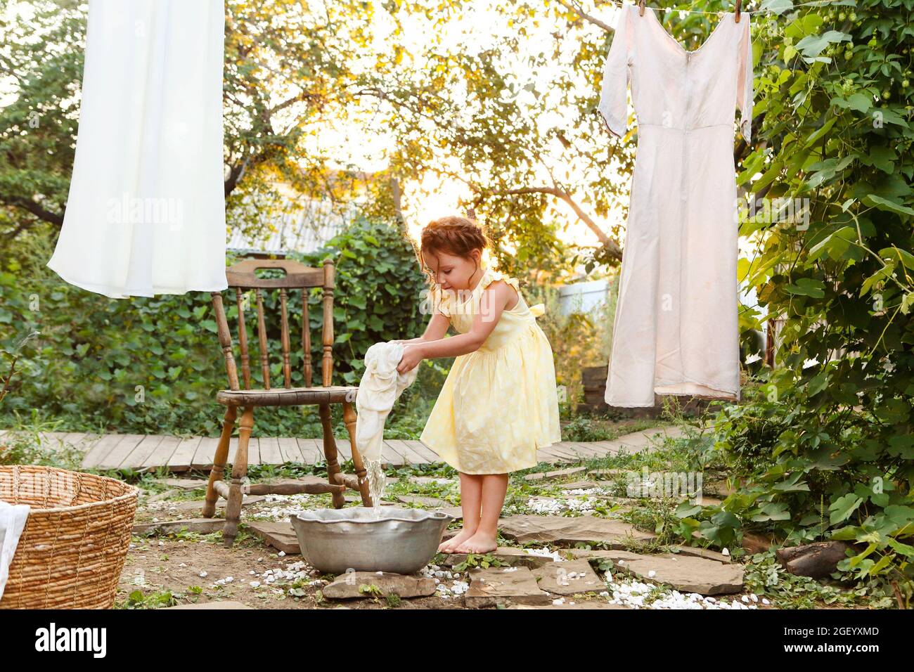 Cute little girl in dress washing white clothes in metal basin in ...