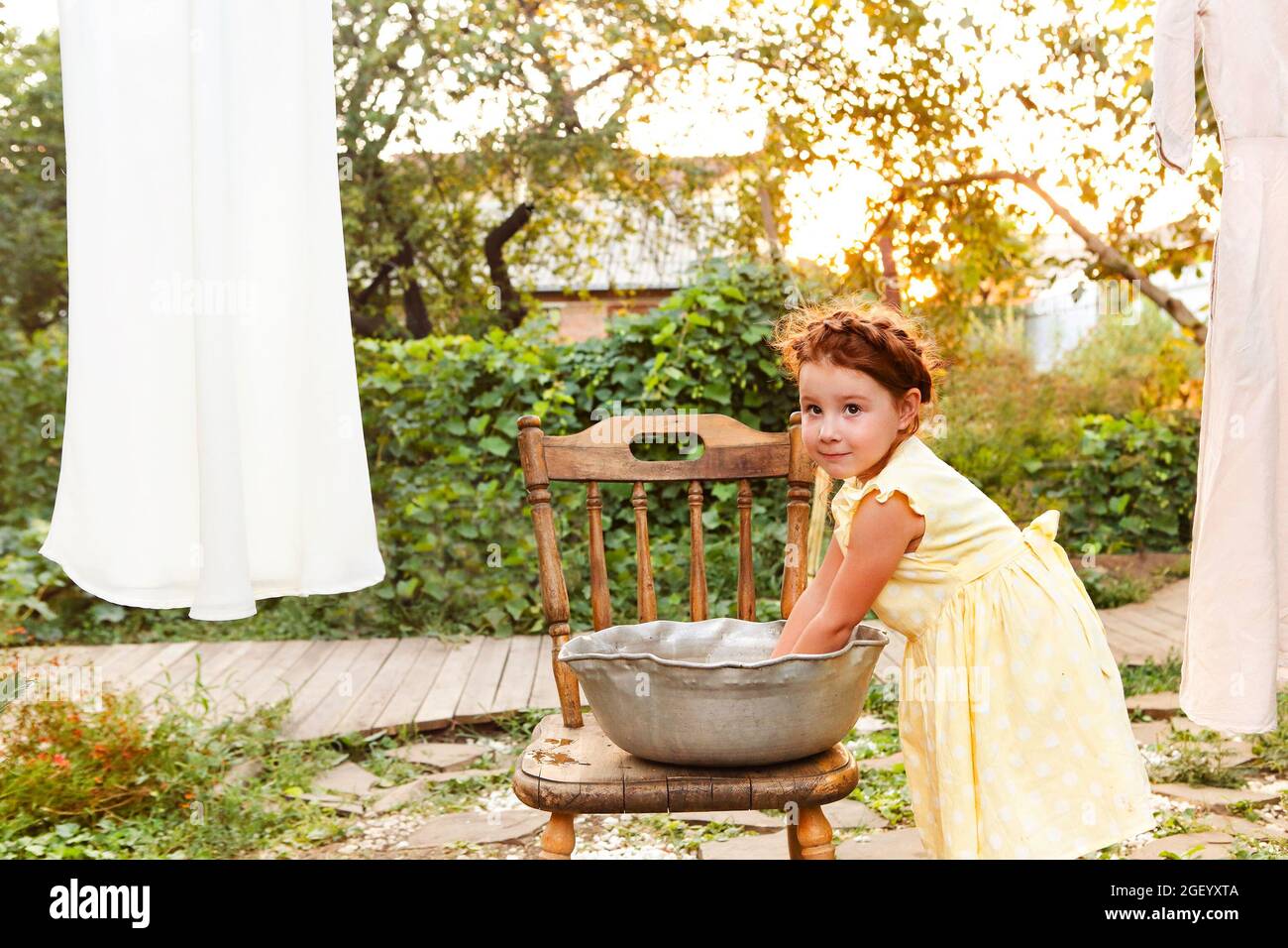 Cute little girl in dress washing white clothes in metal basin in ...