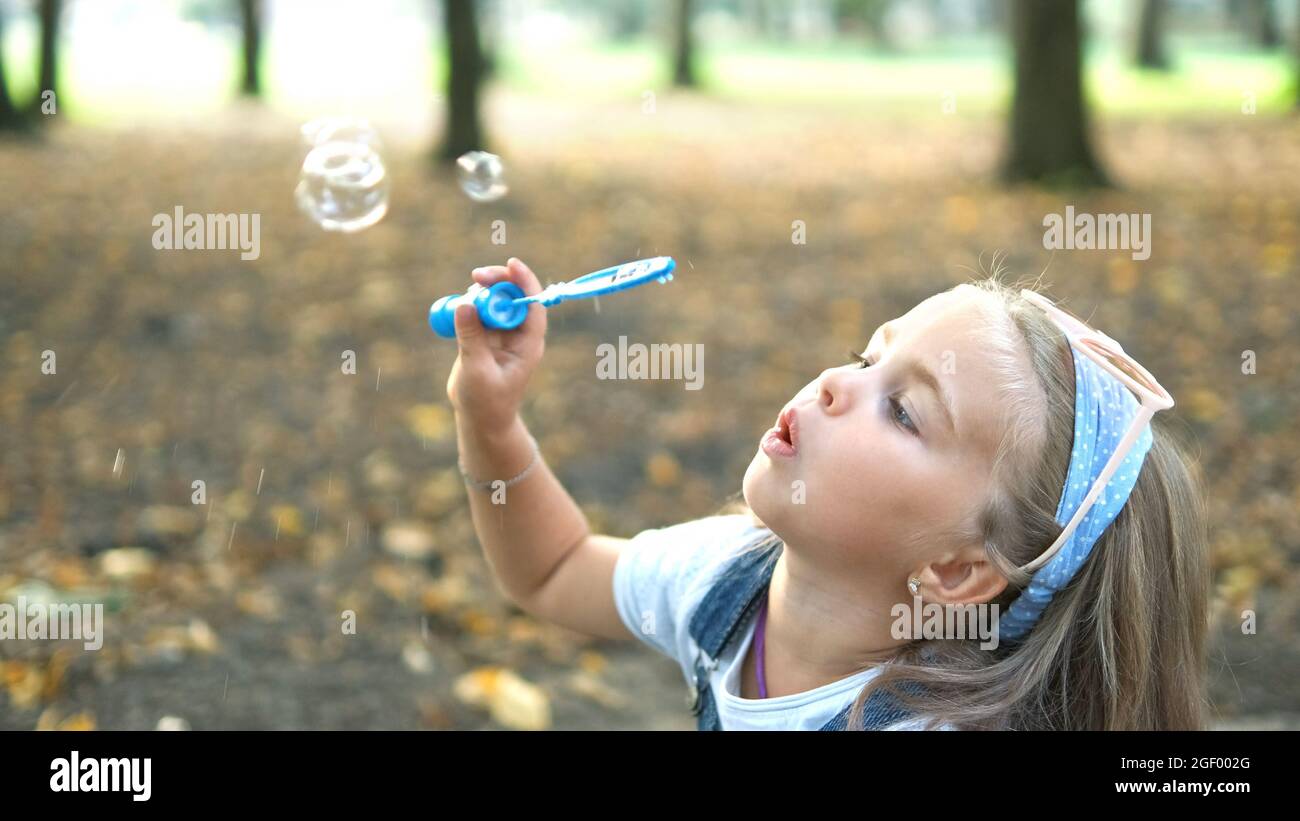 Happy little child girl blowing soap bubbles outside in green park ...