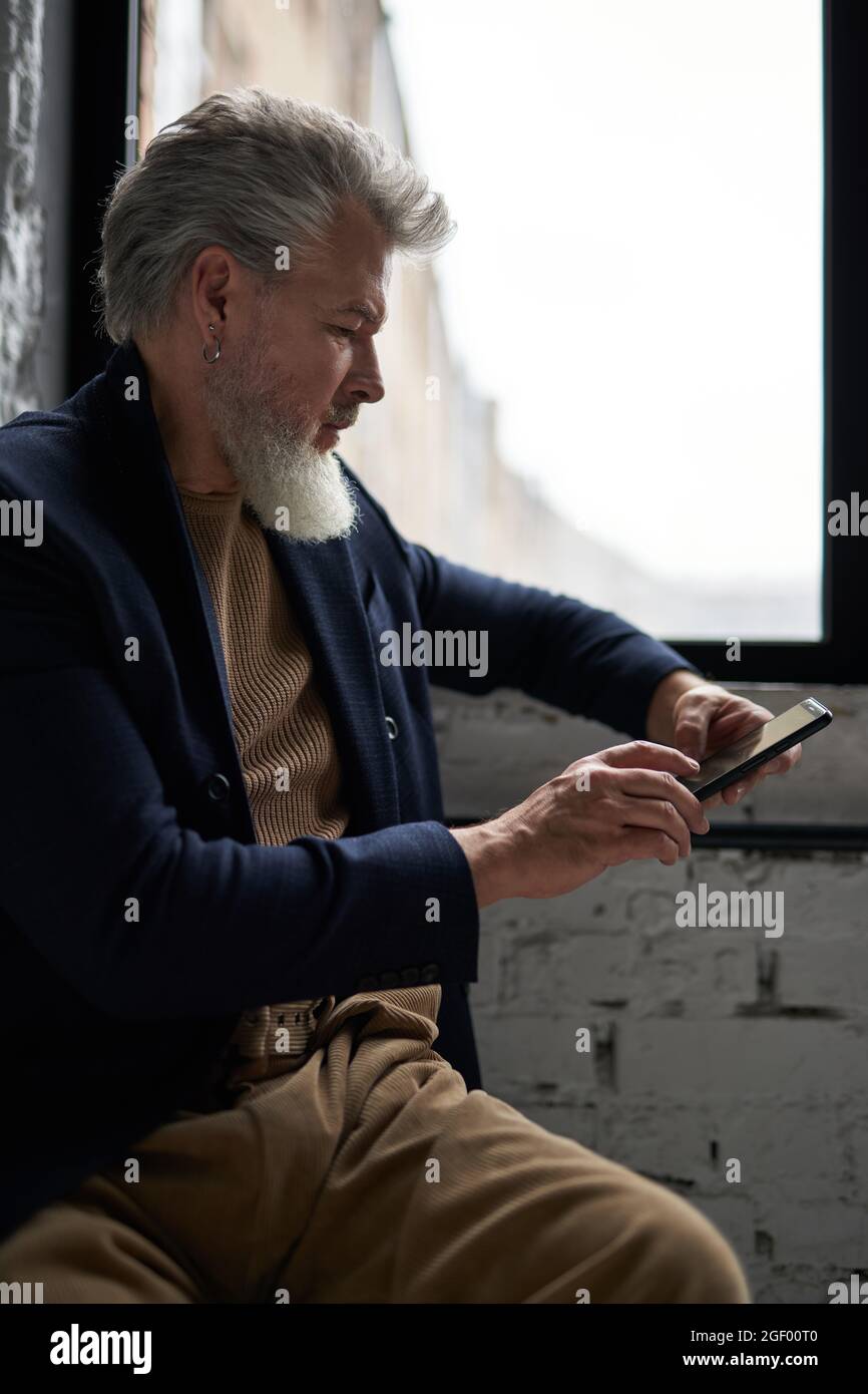 Focused middle aged man in business casual wear using his smartphone ...