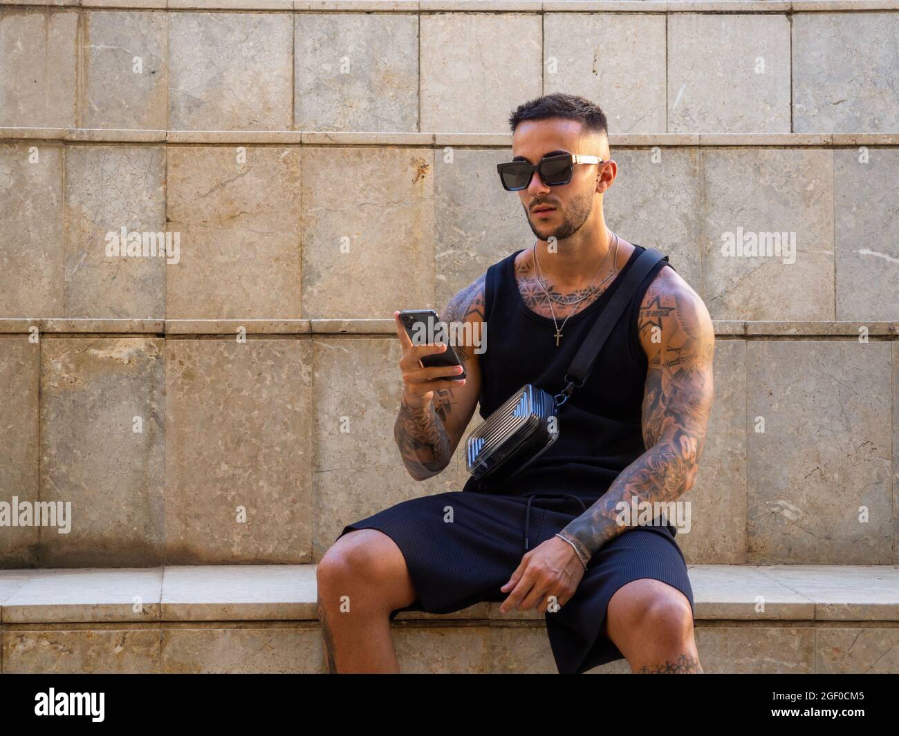 An attractive cool Spanish man with tattoos using his phone while ...