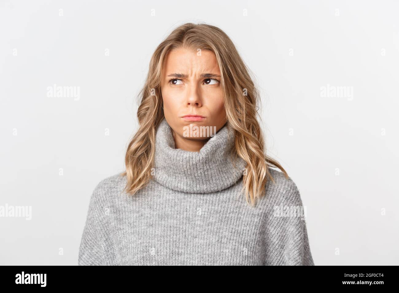 Close-up of gloomy blond girl, pouting and frowning, looking at upper ...