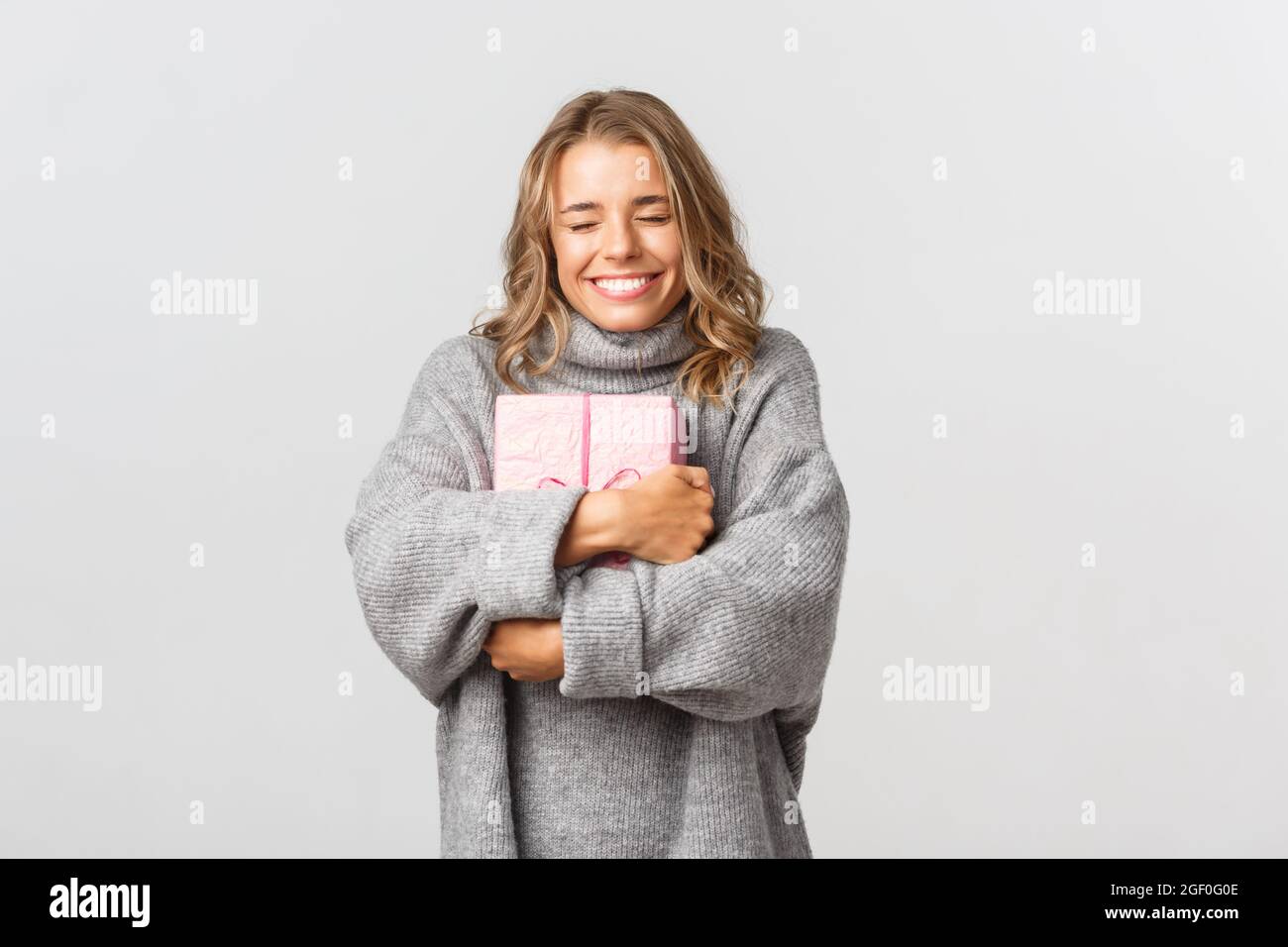 Studio shot of cute smiling girl in grey sweater, hugging her birthday ...