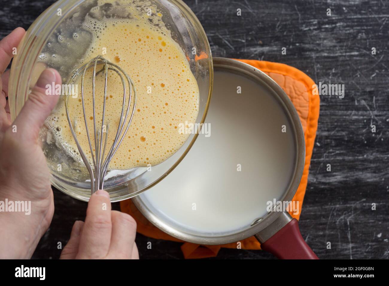 Top view of woman hands putting mix of yolks, starch, sugar and milk in ...