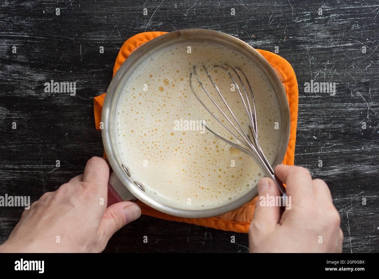 Top view of woman hands stirring hot mix of yolks, starch, sugar and ...