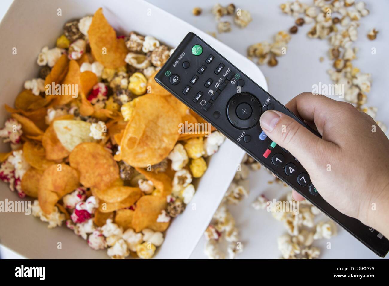 A top view of a hand holding tv remote control against fried popcorn ...
