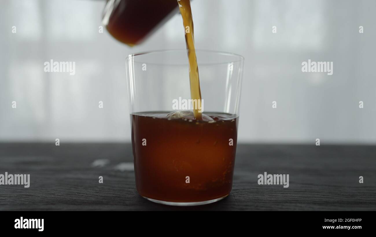 pour cold brew coffee over ice ball in tumbler glass on wood table ...