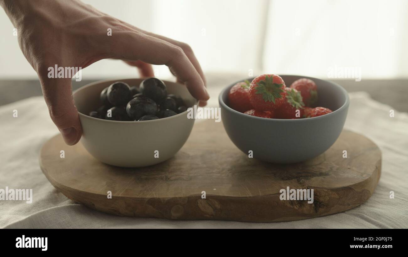 man put fresh strawberries and blueberries in bowls on olive wood board ...
