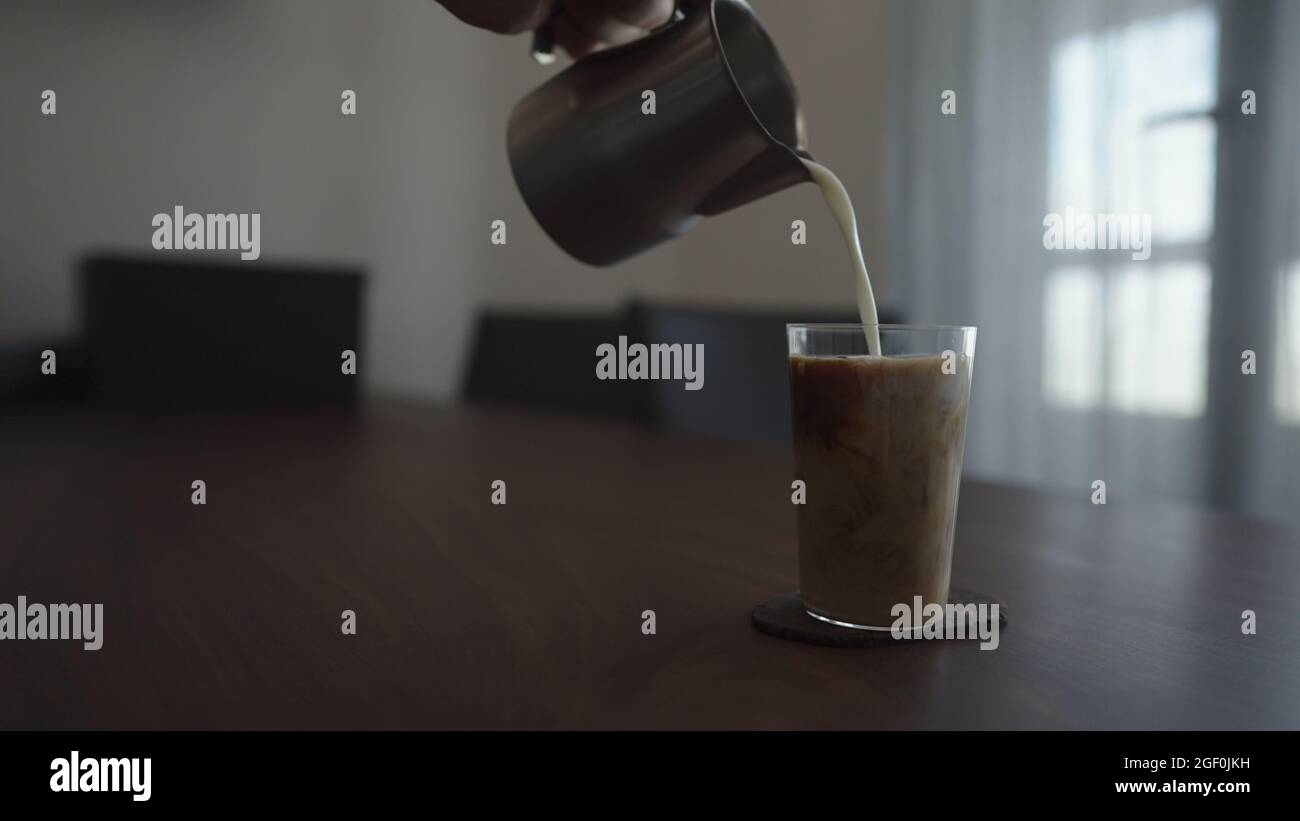 pour milk over cold brew coffee over ice cube in tumbler glass on ...
