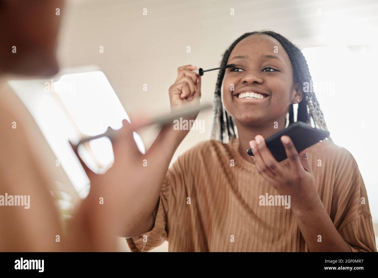 Portrait of young African-American woman putting on mascara while doing ...
