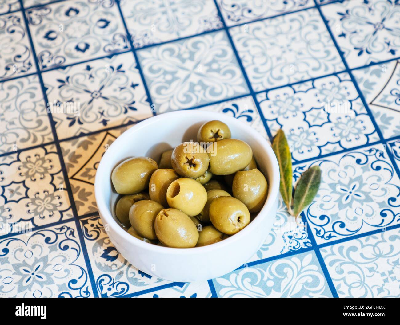 Small white bowl with a green olives snack on a table with traditional ...