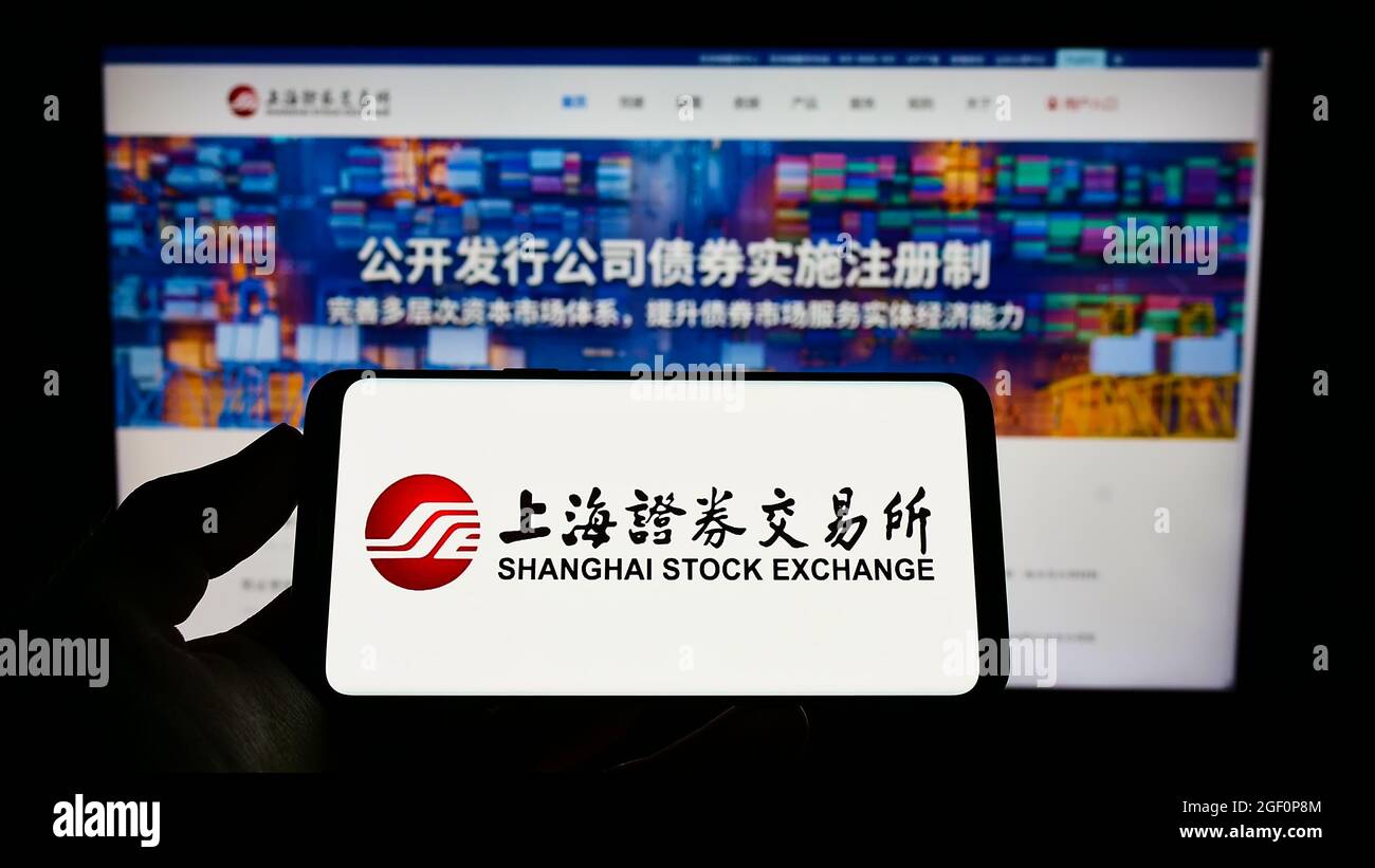 Person holding mobile phone with logo of Chinese Shanghai Stock ...