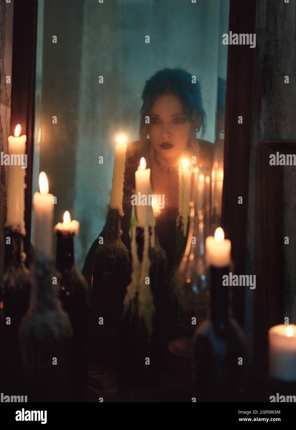 Indoors portrait of beautiful goth girl among candles. Blue-haired ...