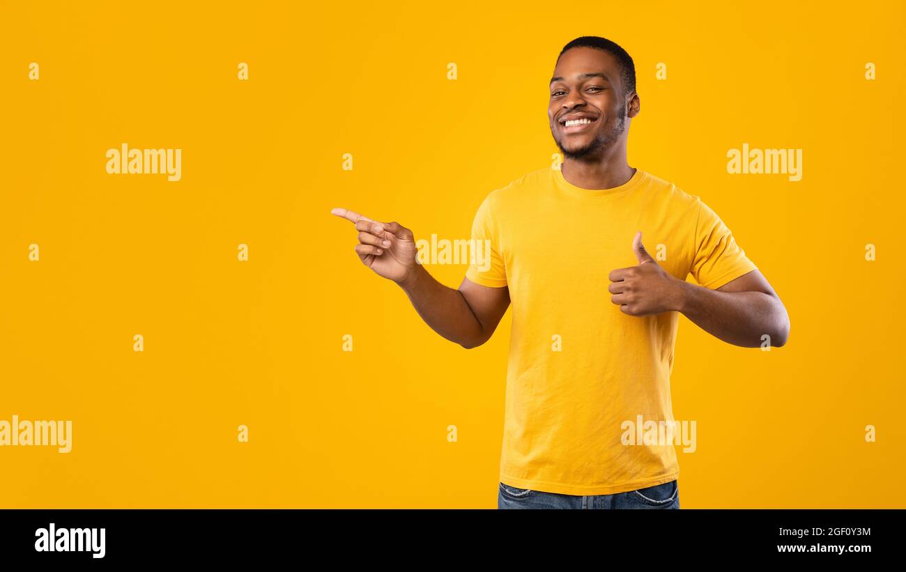 African American Guy Pointing Finger Aside Gesturing Thumbs-Up, Yellow ...