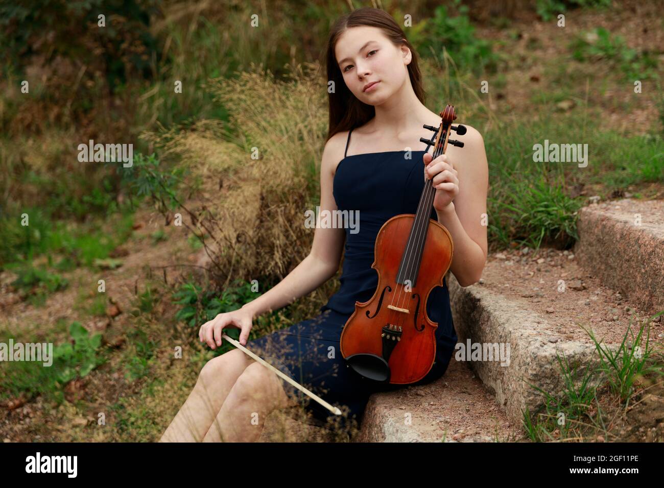 beautiful brown-haired girl of Asian appearance with a violin in nature ...