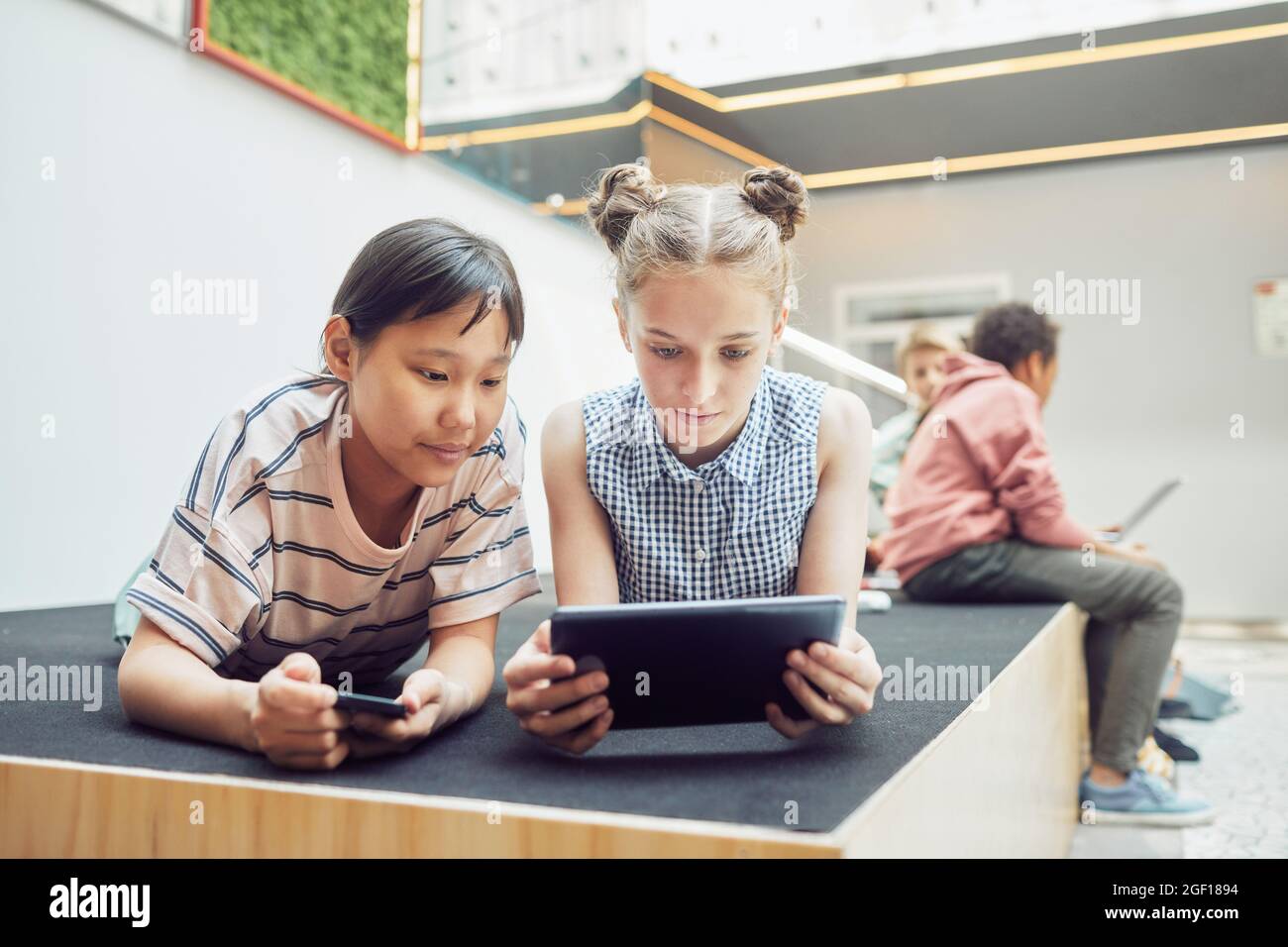 Portrait of two teenage girls using gadgets while relaxing in modern ...