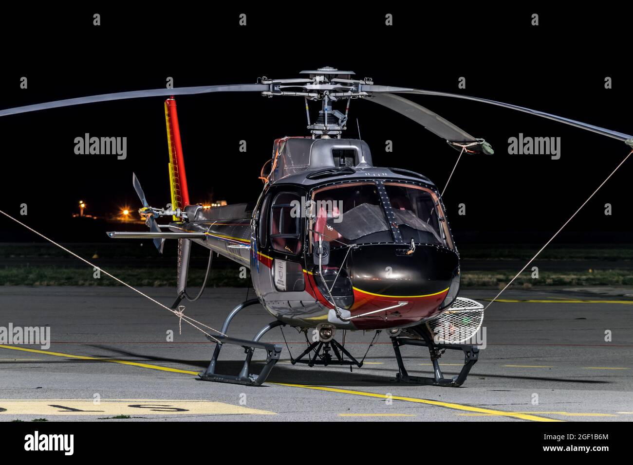 A closeup of a helicopter with tied down rotor blades, against a night ...
