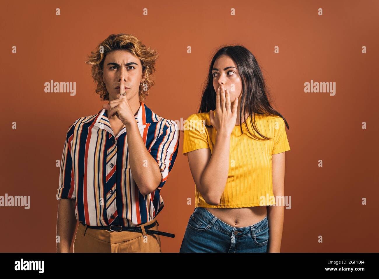 A stylish caucasian man with a hushing gesture and a young surprised ...