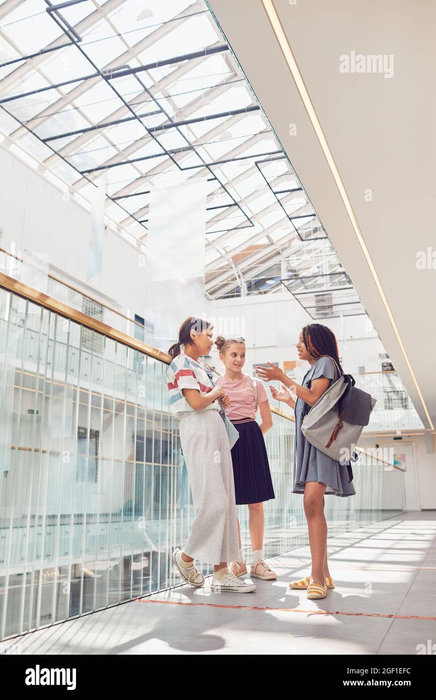 Vertical full length portrait of three schoolgirls chatting in school ...