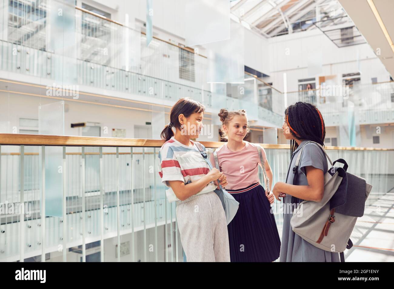 Portrait of three schoolgirls chatting in school while standing in ...