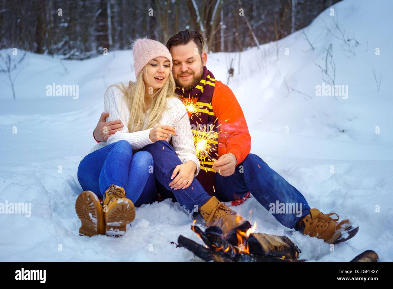 Happy couple man and woman hugging in winter in the forest by the fire ...