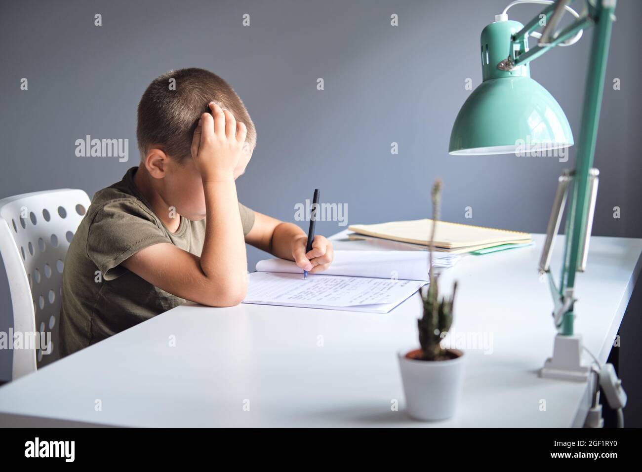 The schoolboy sitting at the table and doing schoolwork at home ...
