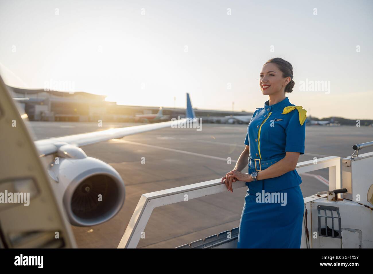 Pretty air stewardess in blue uniform smiling away, standing outdoors ...