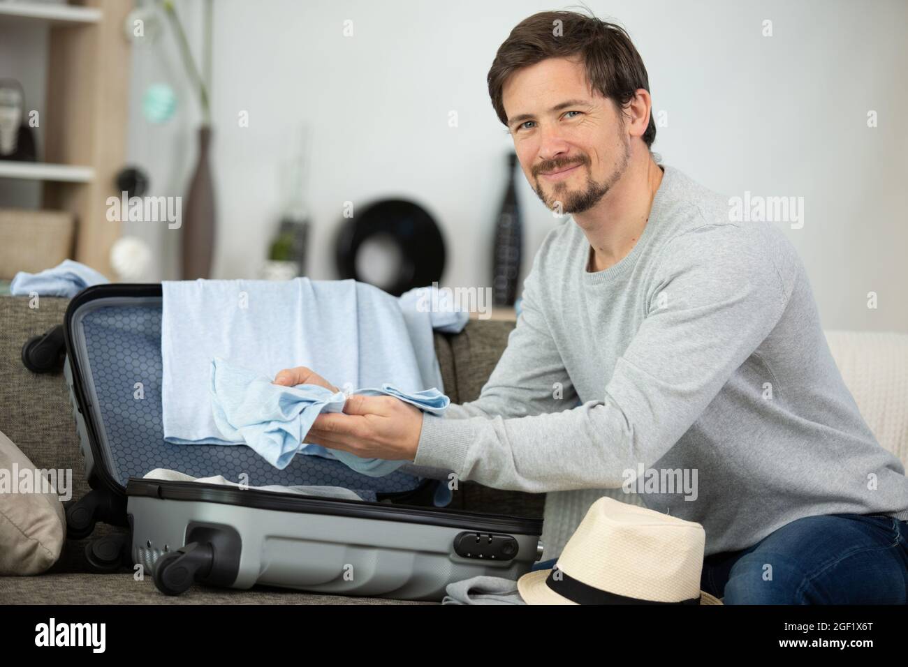 young man packing suitcase and smiling at camera Stock Photo - Alamy