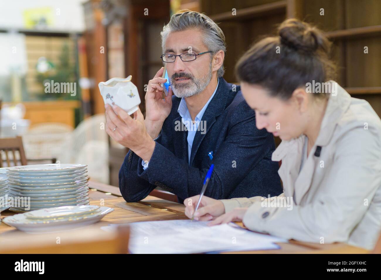 antique dealer inspecting object assistant making notes beside him ...