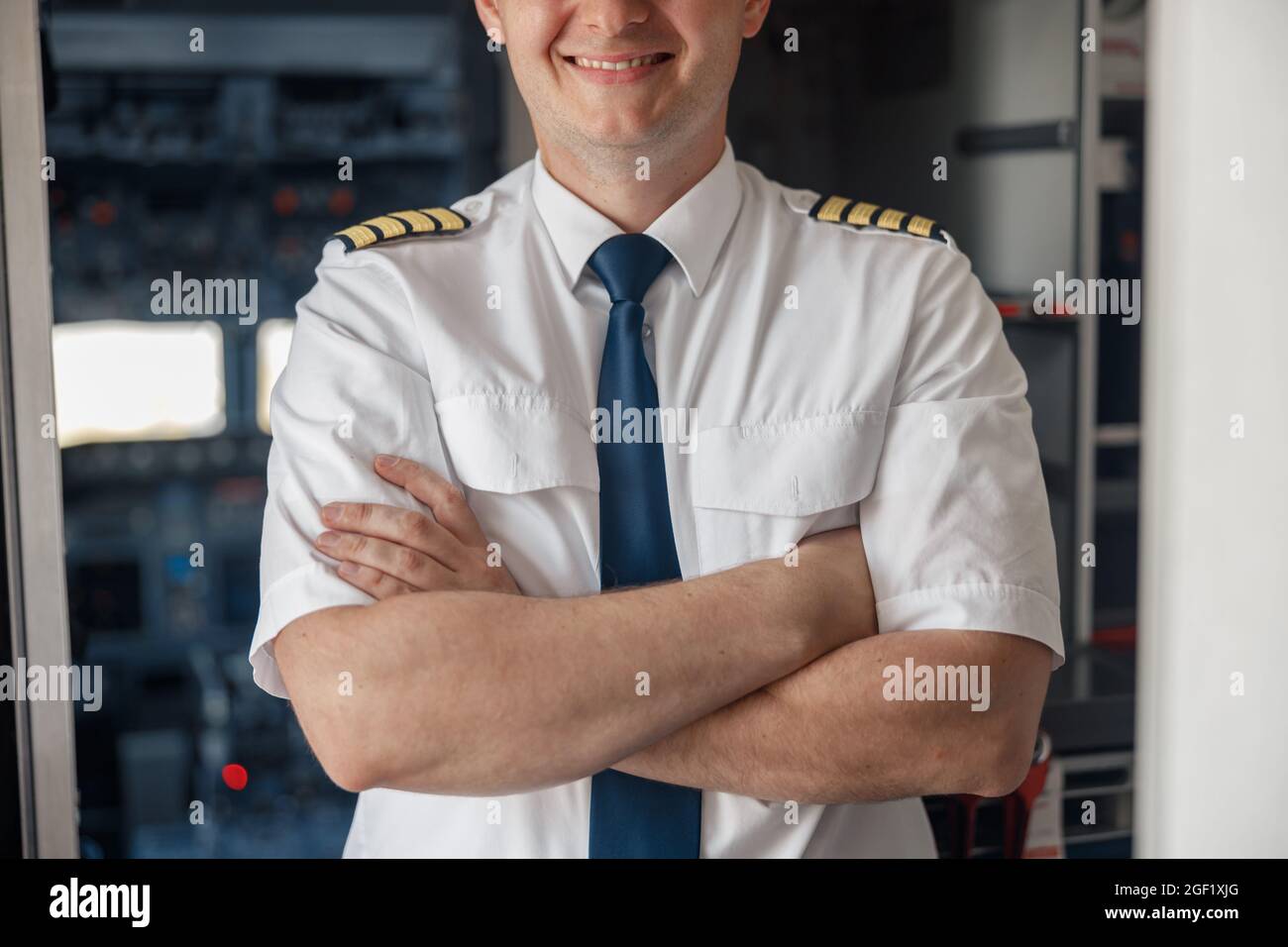Cropped portrait of male pilot in uniform keeping arms crossed and ...