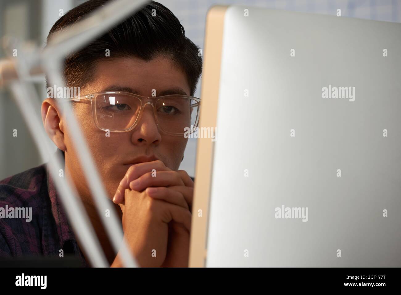Face of pensive young software developer looking at computer screen ...
