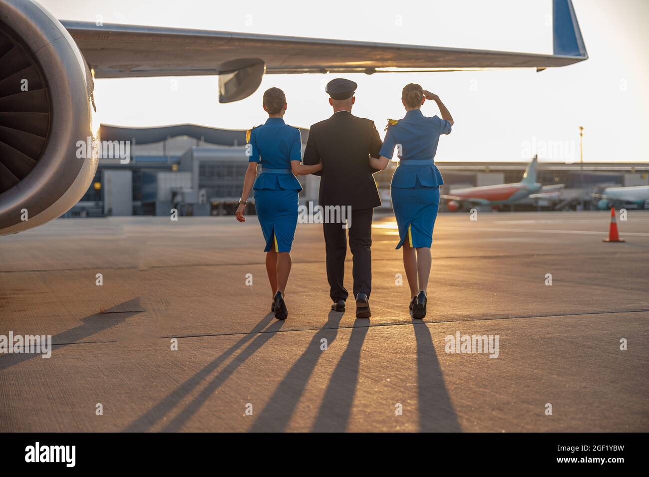 Full length shot of professional pilot walking together with two female ...