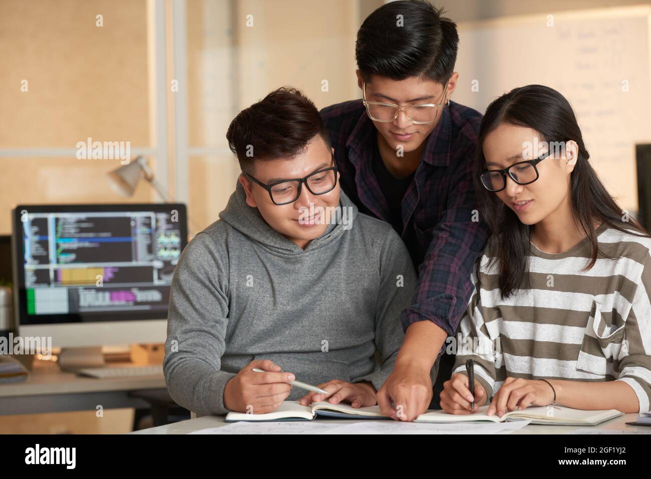 Smart positive college student helping friends with doing project for ...