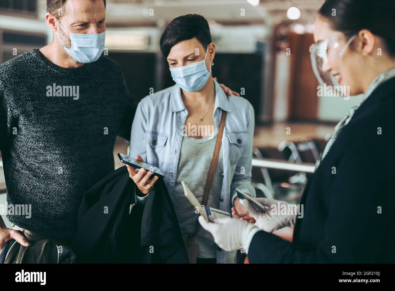 Tourist couple in face masks at check-in counter with airport staff ...