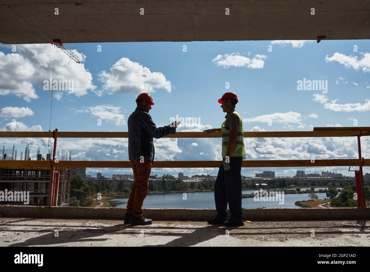 Backlit side view at two construction workers discussing project while ...