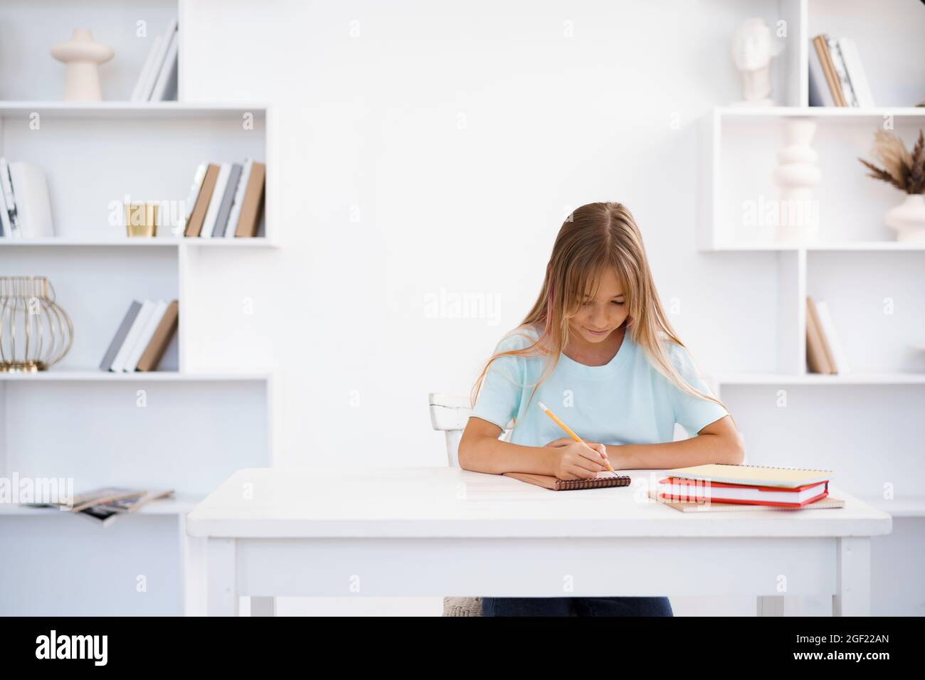 Teenage girl making notes in notepad, doing homework at table at home ...