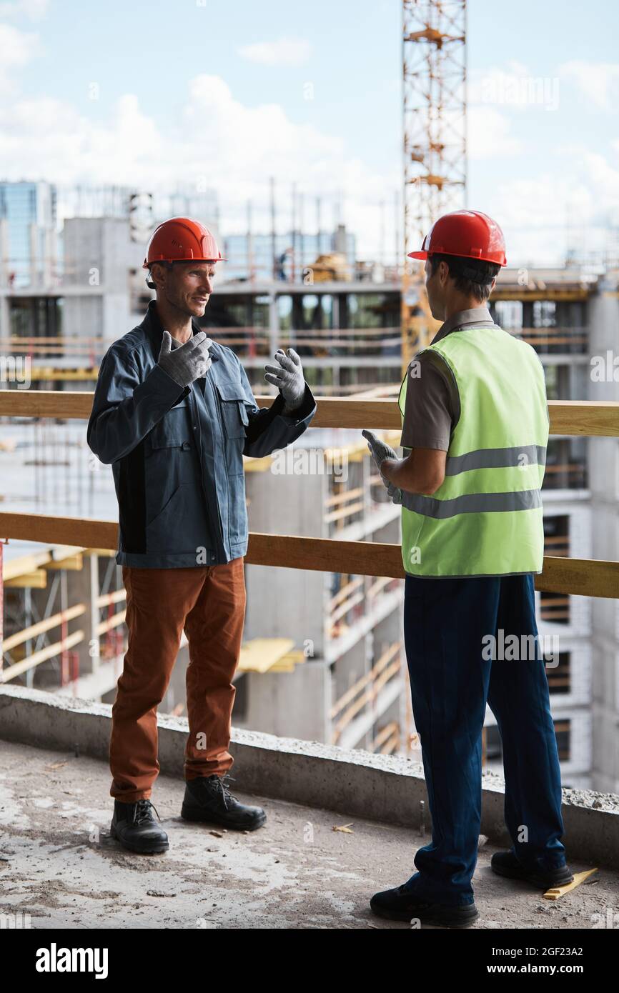 Vertical full length portrait of two construction workers discussing ...