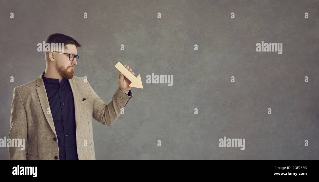 Sad businessman holding arrow that's pointing down on grey copy space ...
